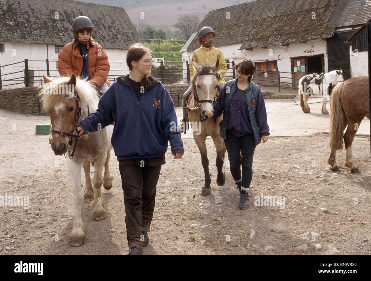 Instructors teaching school children how to ride a pony Stock Photo - Alamy