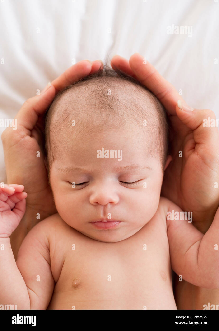 Parent's hands wrapped around sleeping baby's head Stock Photo - Alamy