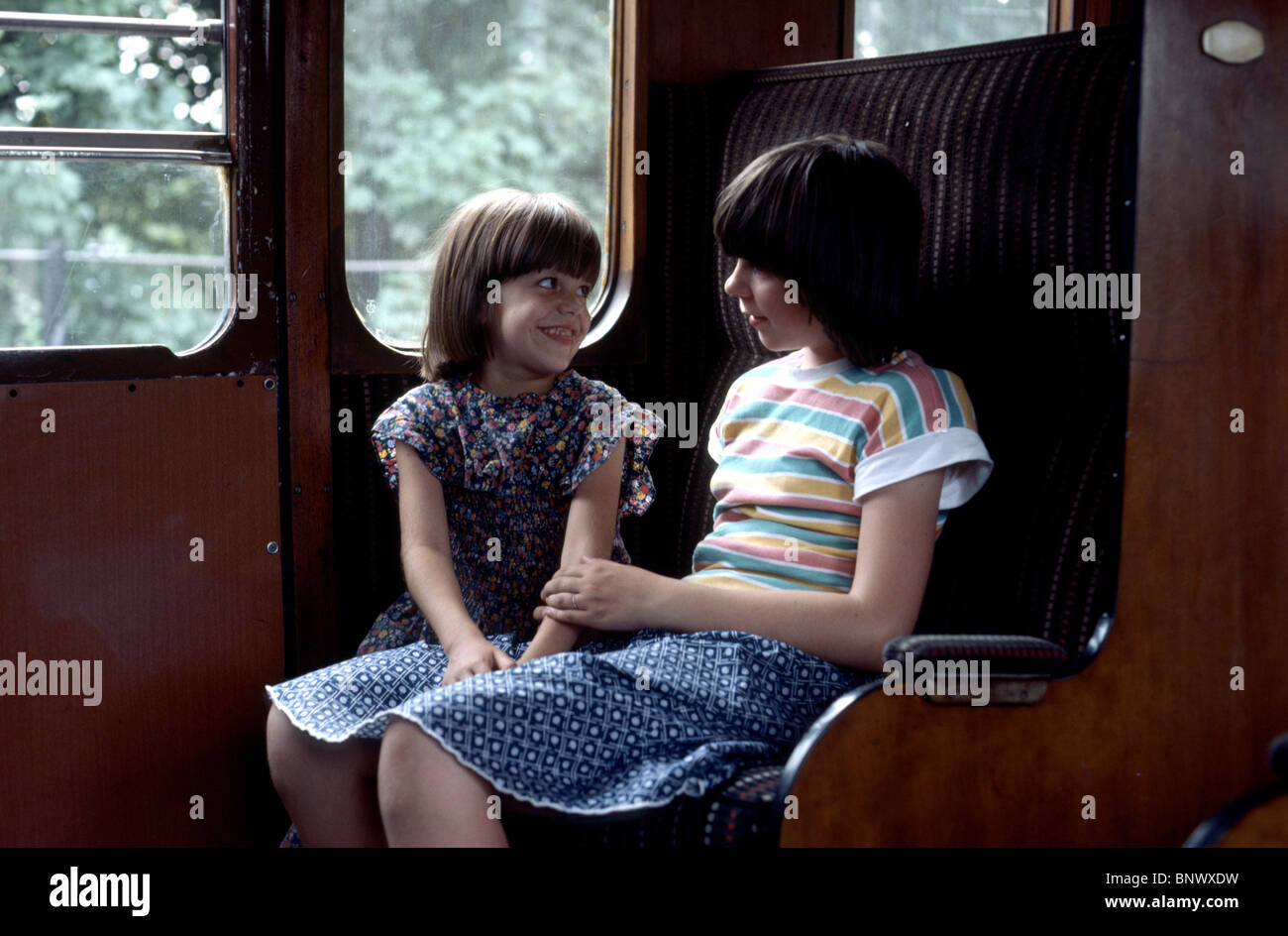 two young girls in an old commuter train laughing and talking together ...
