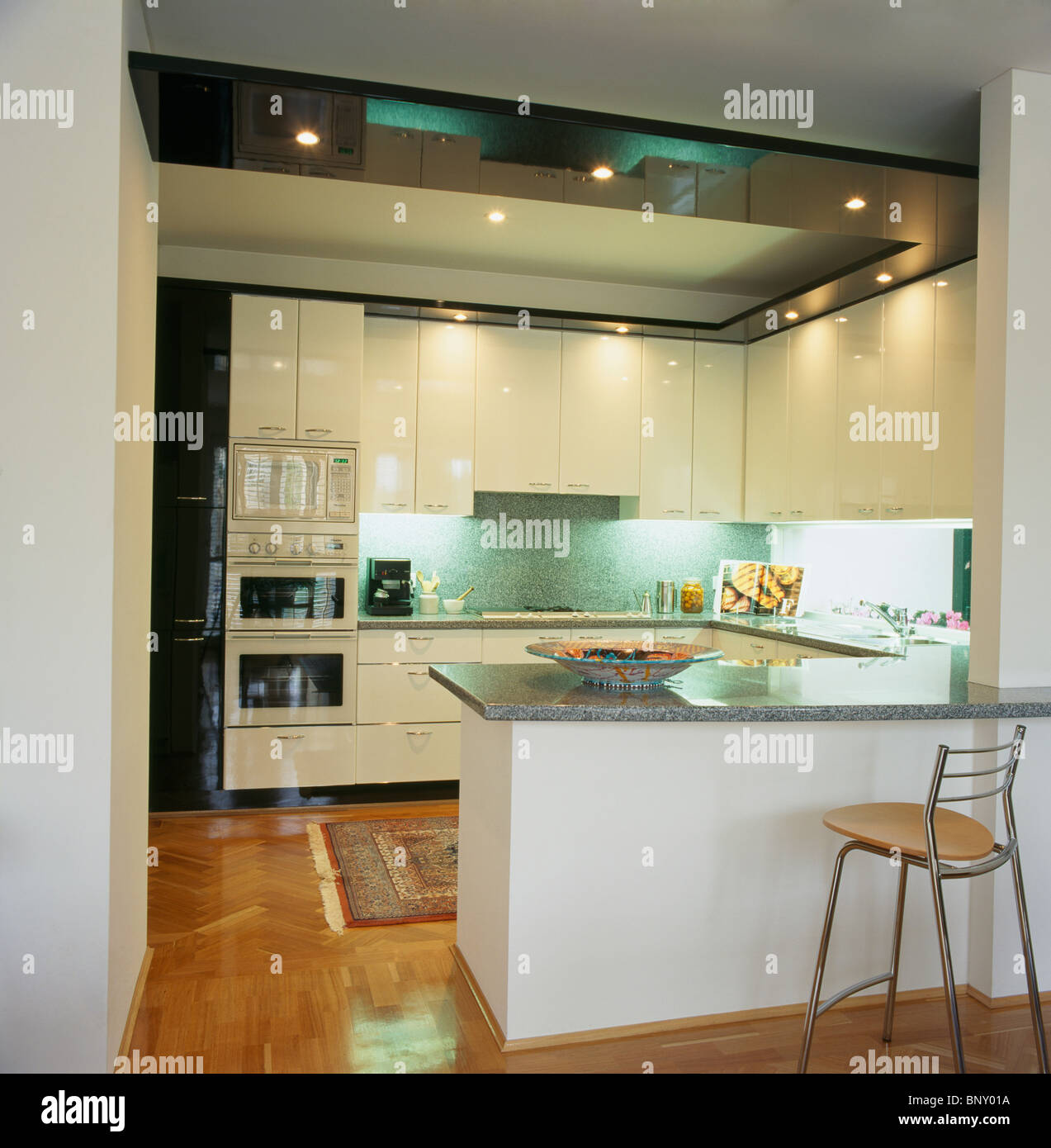 Chair at granite-topped peninsular unit in modern white kitchen with ...
