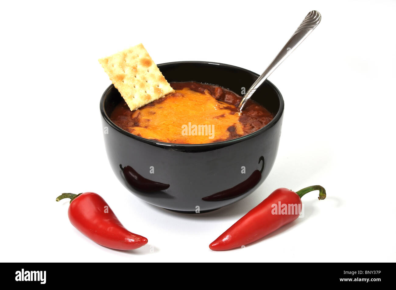 Bowl of chili with melted cheese, cracker, red cayenne peppers, and ...
