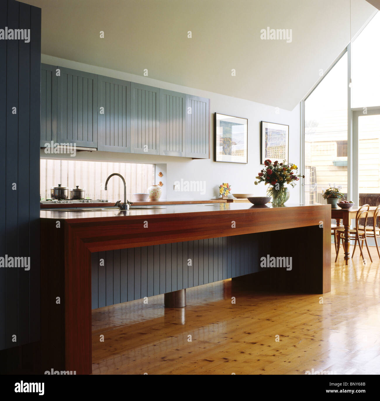 Long wood island unit in open-plan modern kitchen with pale blue ...