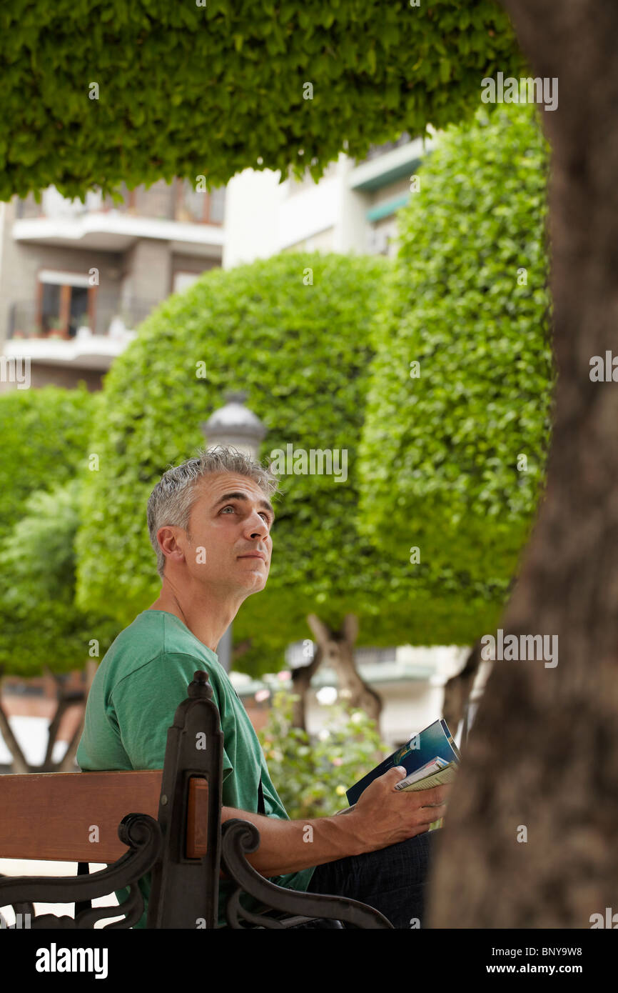 Man sitting on bench holding a book Stock Photo - Alamy