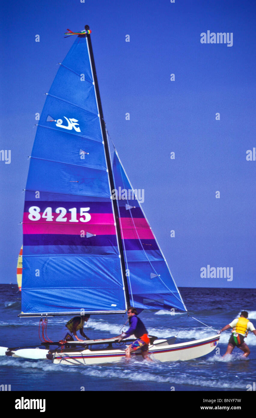 Three men attempt to launch small sail boat in ocean waves Stock Photo ...