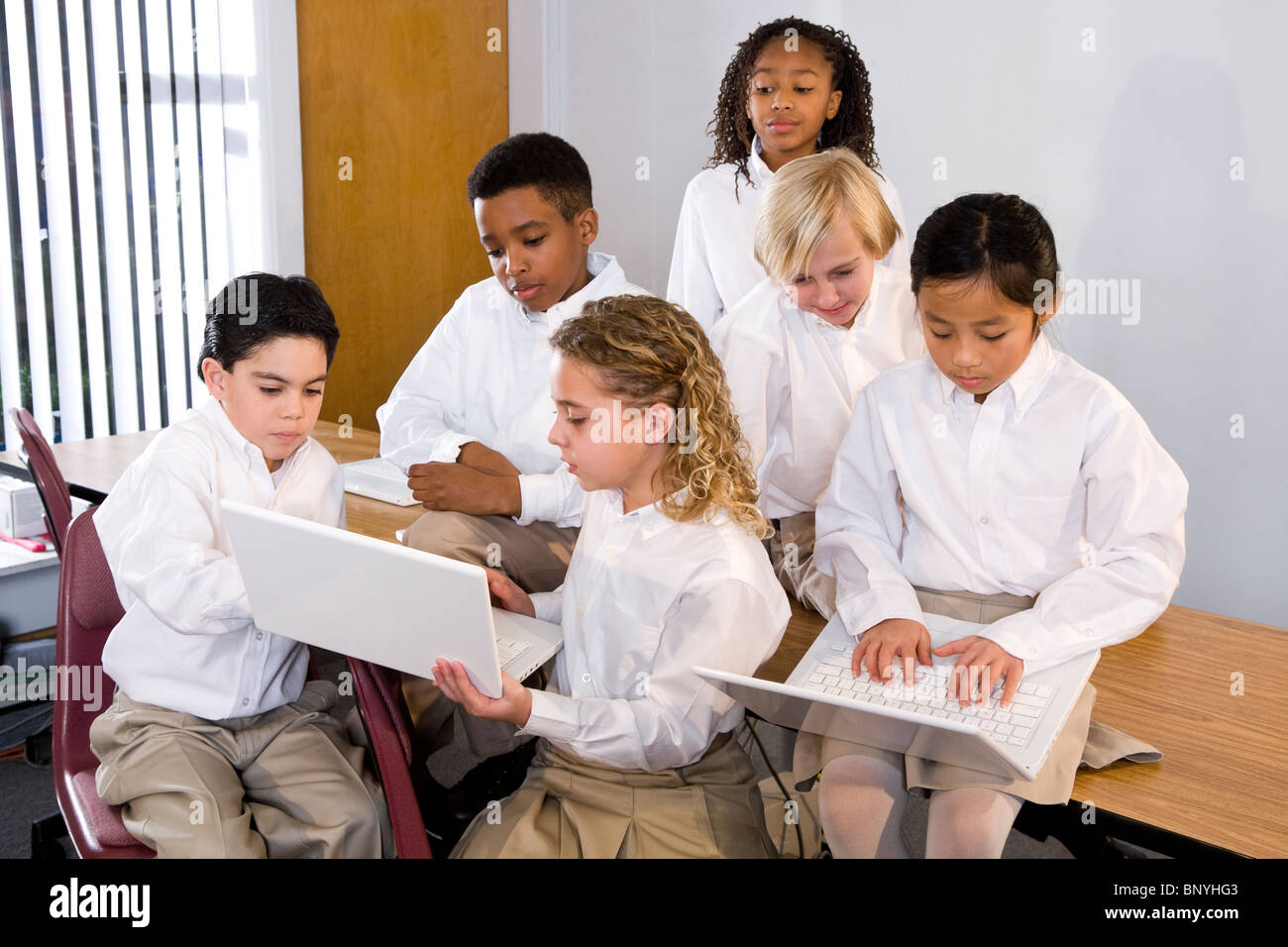 Diverse group of elementary school students in class using laptops ...