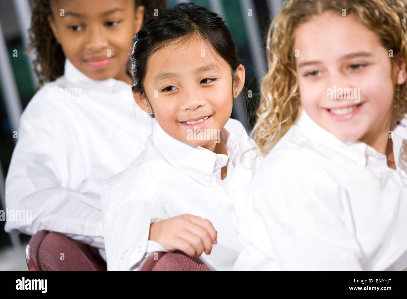 Happy young school girls sitting in a row looking over shoulder Stock ...