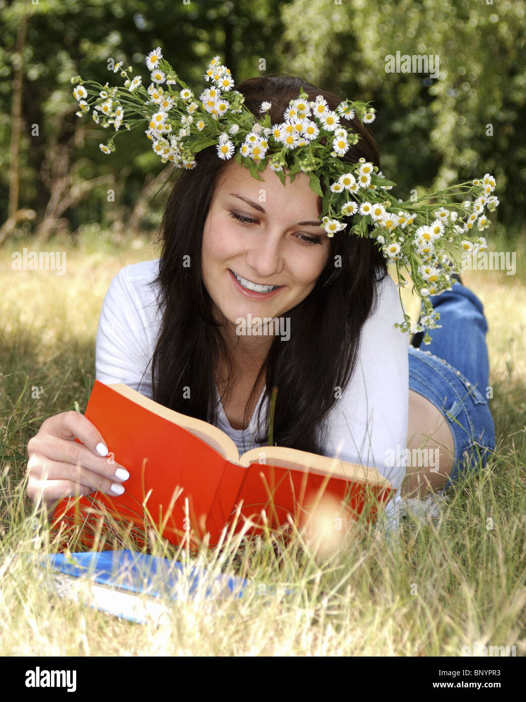 Happy smiling girl in garland reading book outside Stock Photo - Alamy