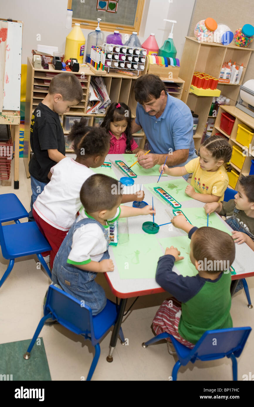 Male preschool teacher sitting with students at a table painting with ...