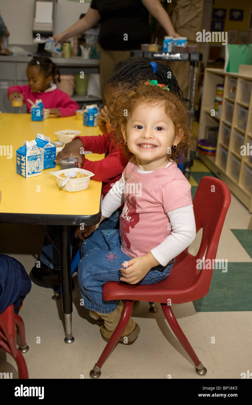 Preschool girl eating breakfast and smiling at the camera in the school ...