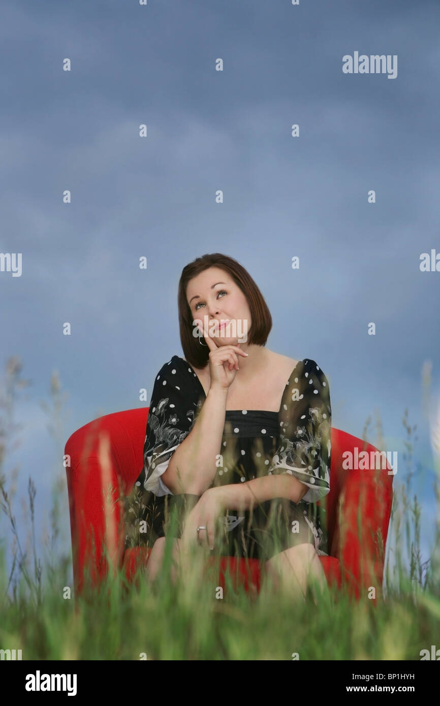 A Woman Sitting In A Red Chair In A Field In A Thinking Pose Stock ...