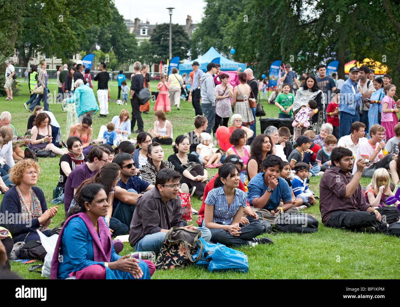 Multi Ethnic Crowd Of People Sitting On Grass Enjoying Watching A Performance At The 2010