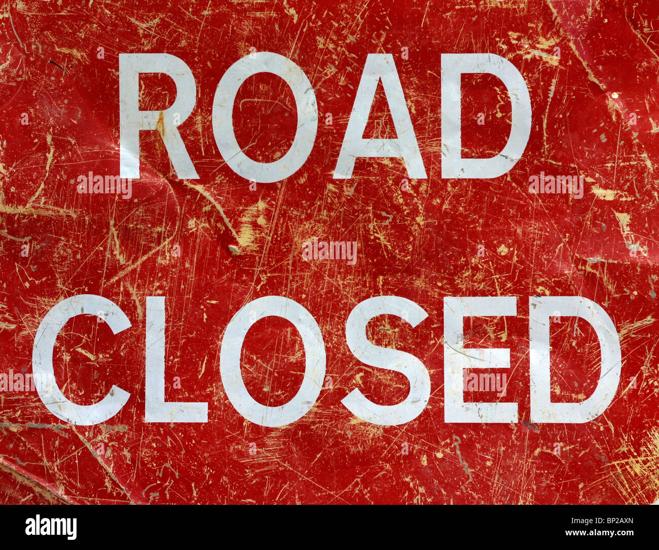 Red, metal "road closed" sign covered in small scratches and dents ...