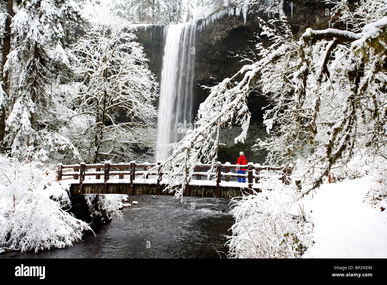 A Person Standing On A Snow Covered Bridge Watching A Waterfall In ...
