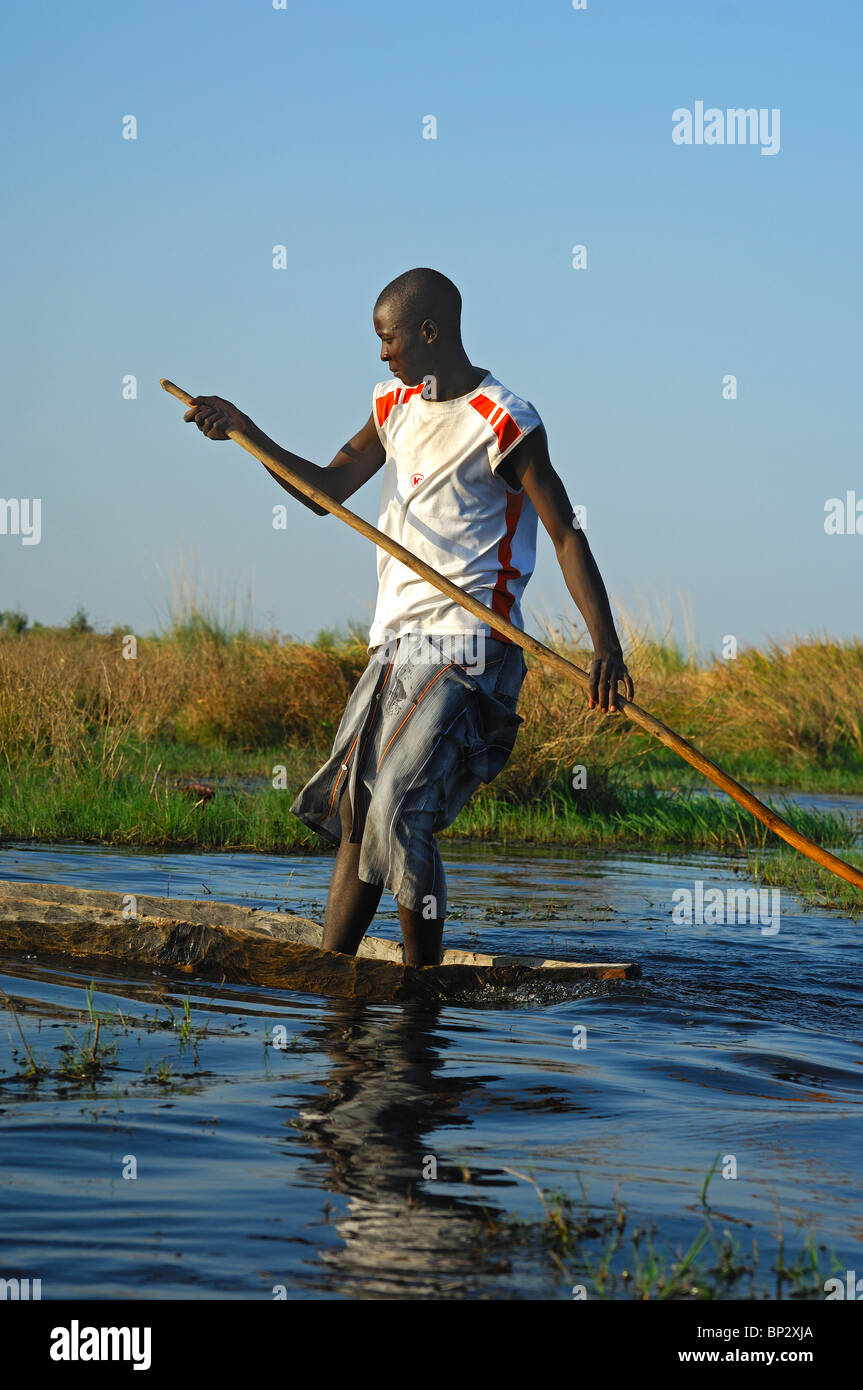 Young man of the local Bayei community punting with a pole in a ...
