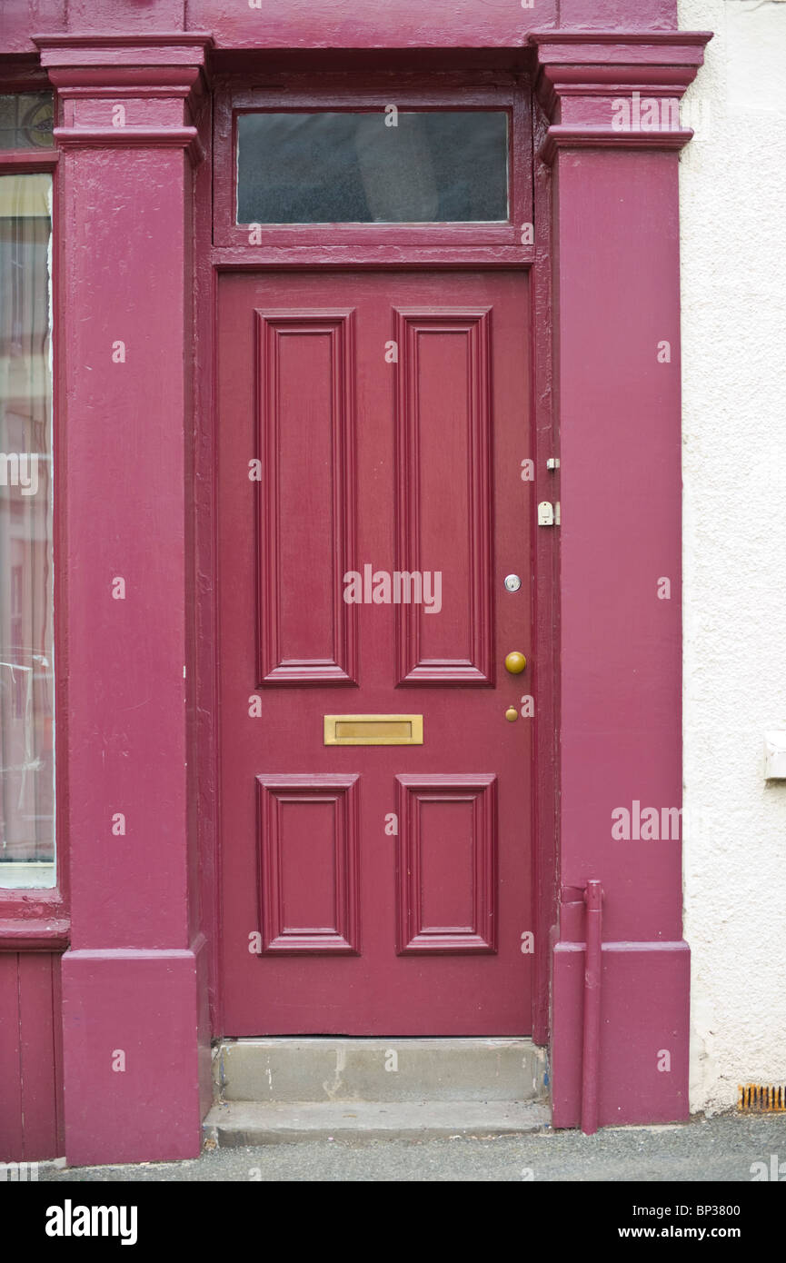 Red painted wooden paneled front door and surround with brass knob and ...