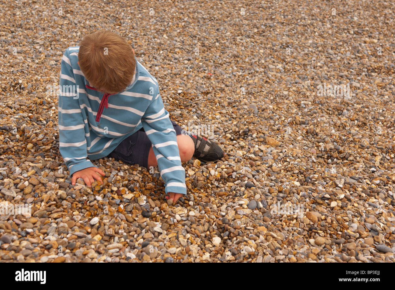 A MODEL RELEASED picture of a 6 year old boy picking up stones near the ...