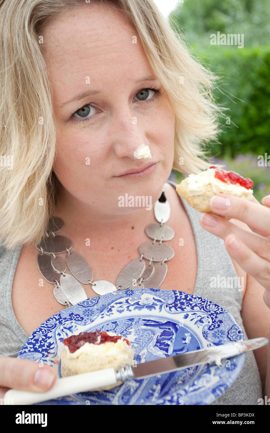 female with cream on her nose eating scones with strawberry jam and ...