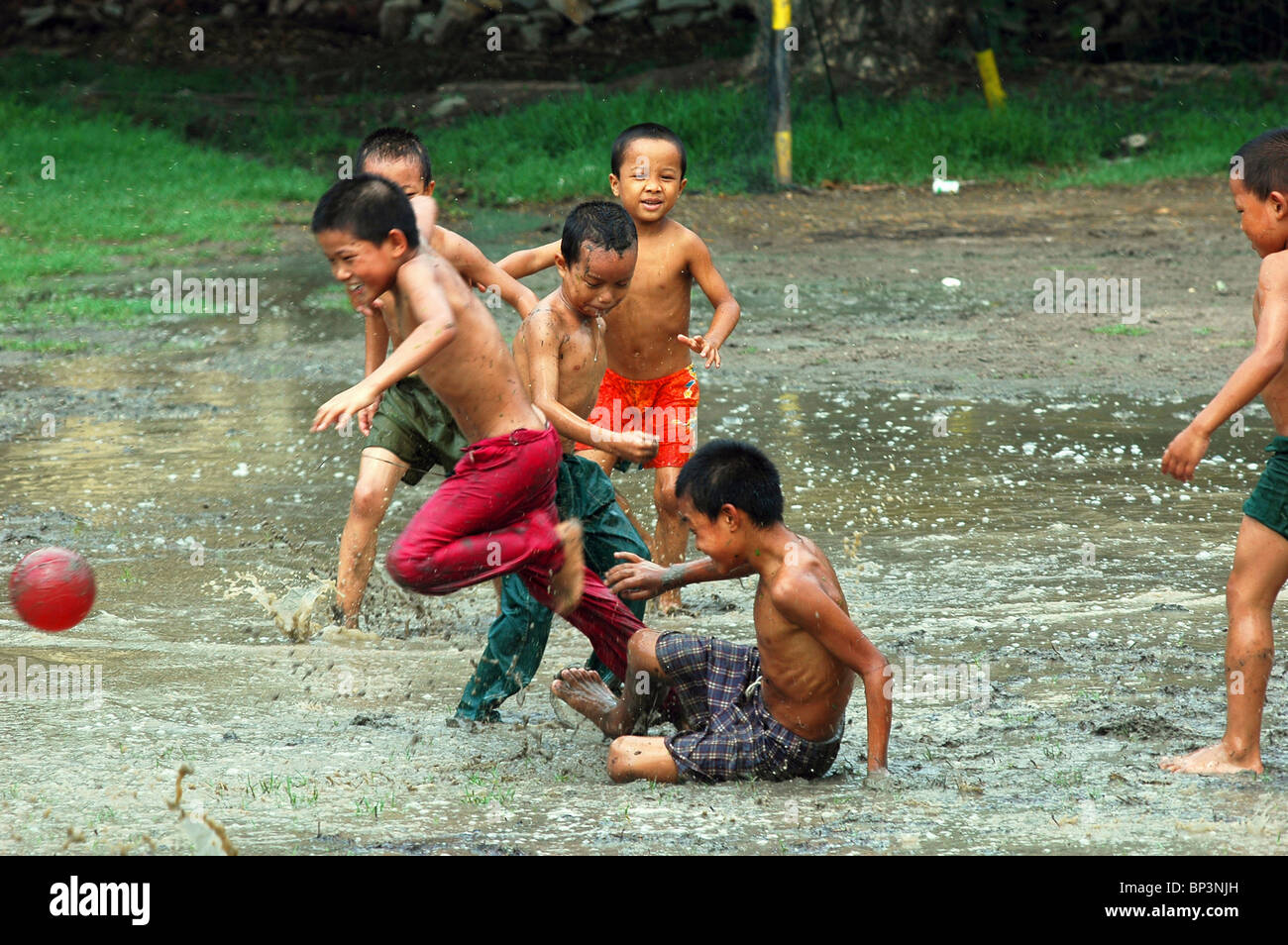 Myanmar, Mandalay, Asian boys playing football on a field soaked by ...