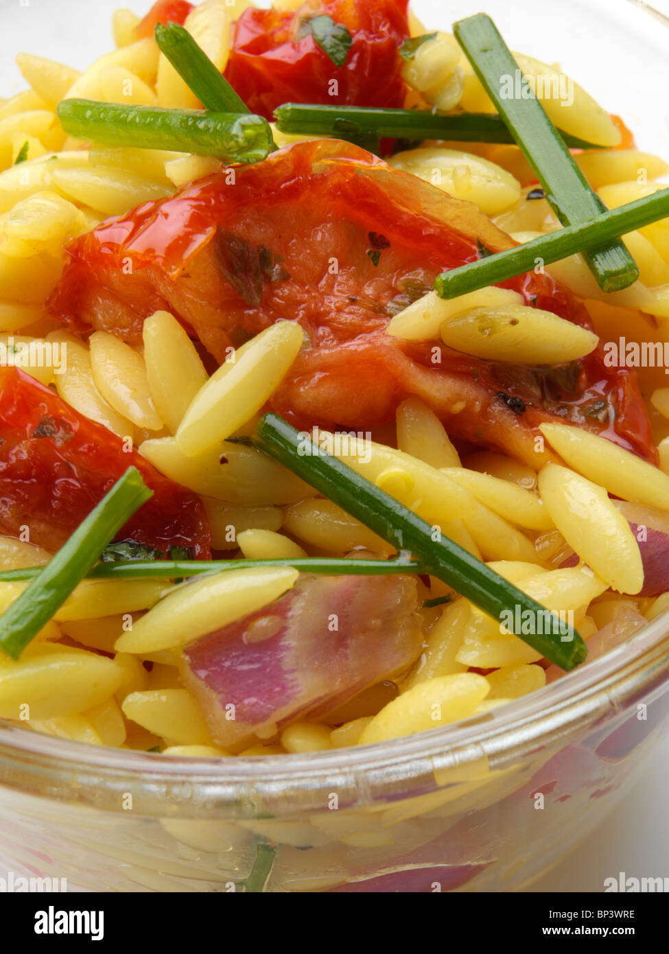 Orzo rice shaped pasta sun dried tomato salad in glass bowl on a white ...