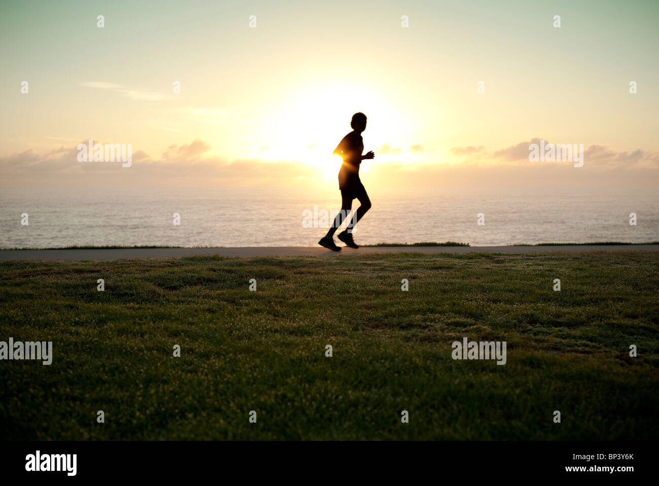 A silhouette of a jogger running alone with sun on horizon Stock Photo ...
