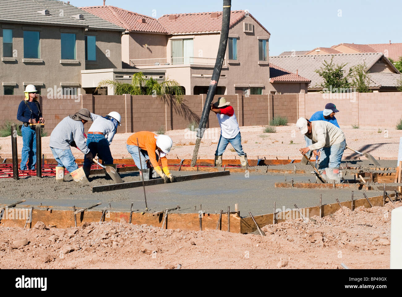 A crew of construction workers pour a concrete pad for a new house ...