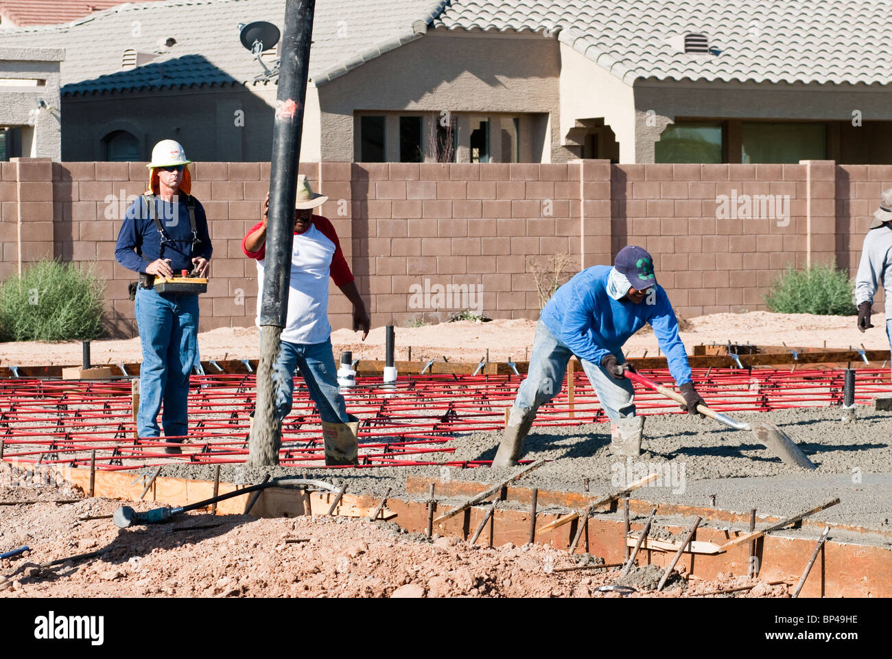 A crew of construction workers pour a concrete pad for a new house ...
