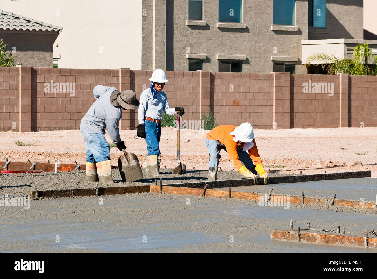 A crew of construction workers pour a concrete pad for a new house ...