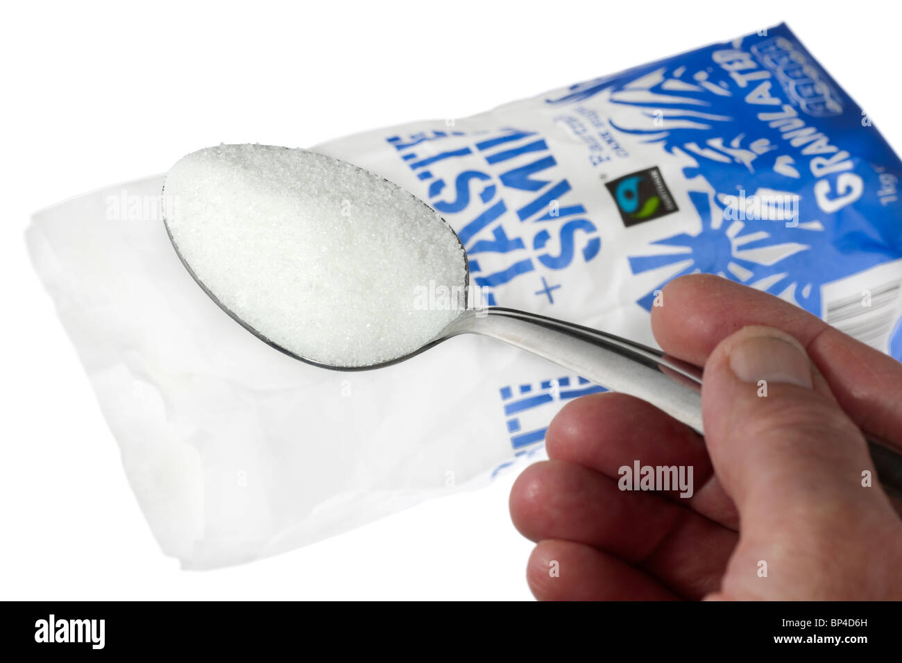 Hand lifting a tablespoonful of granulated sugar from a paper sugar bag ...