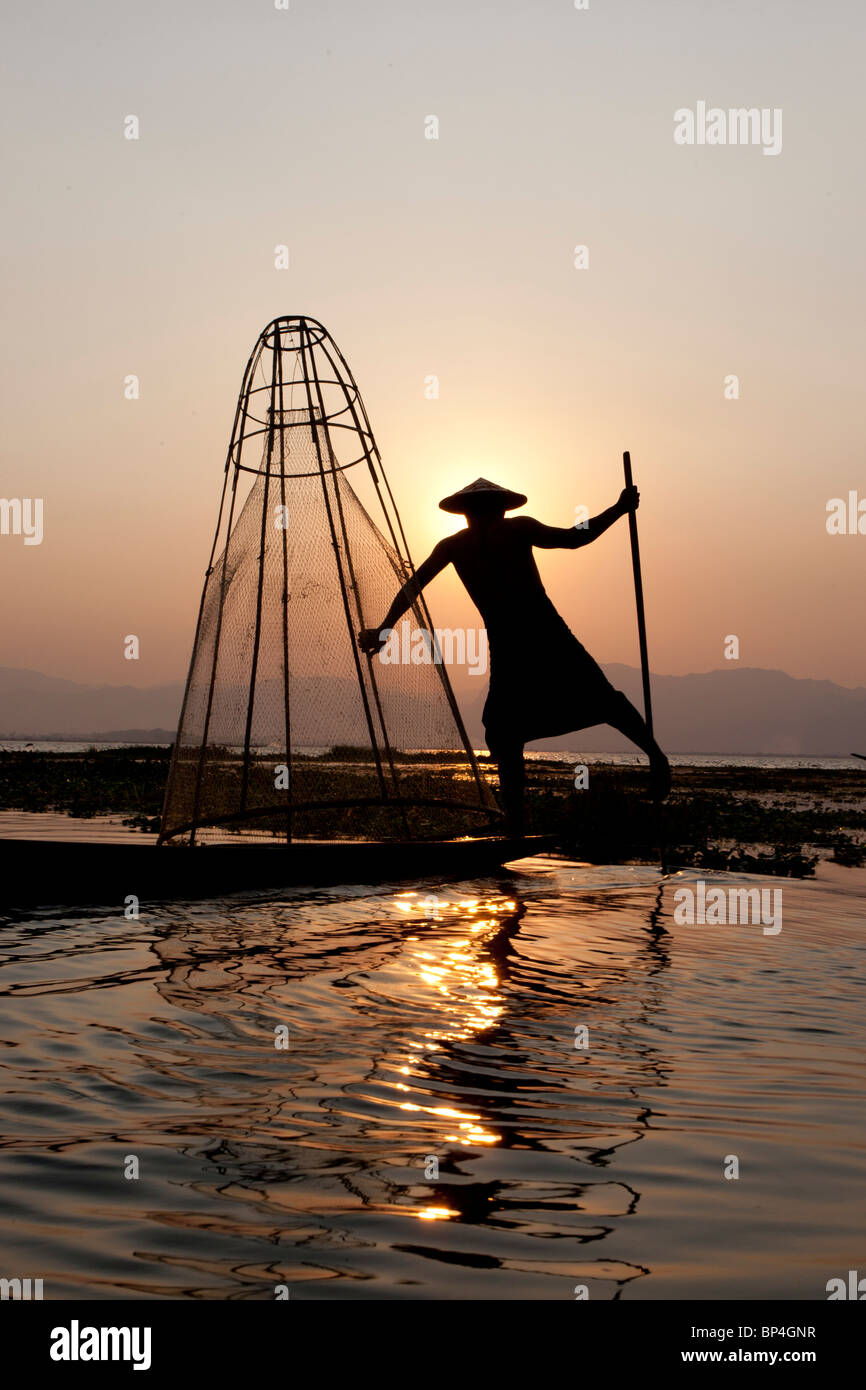 A leg rowing fisherman maneuvers his teak wood canoe above the fish on ...