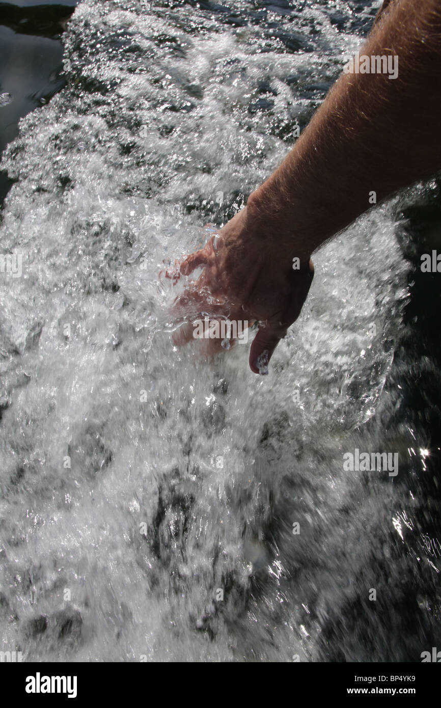 A man's hand draped over the side of a boat letting the water run ...