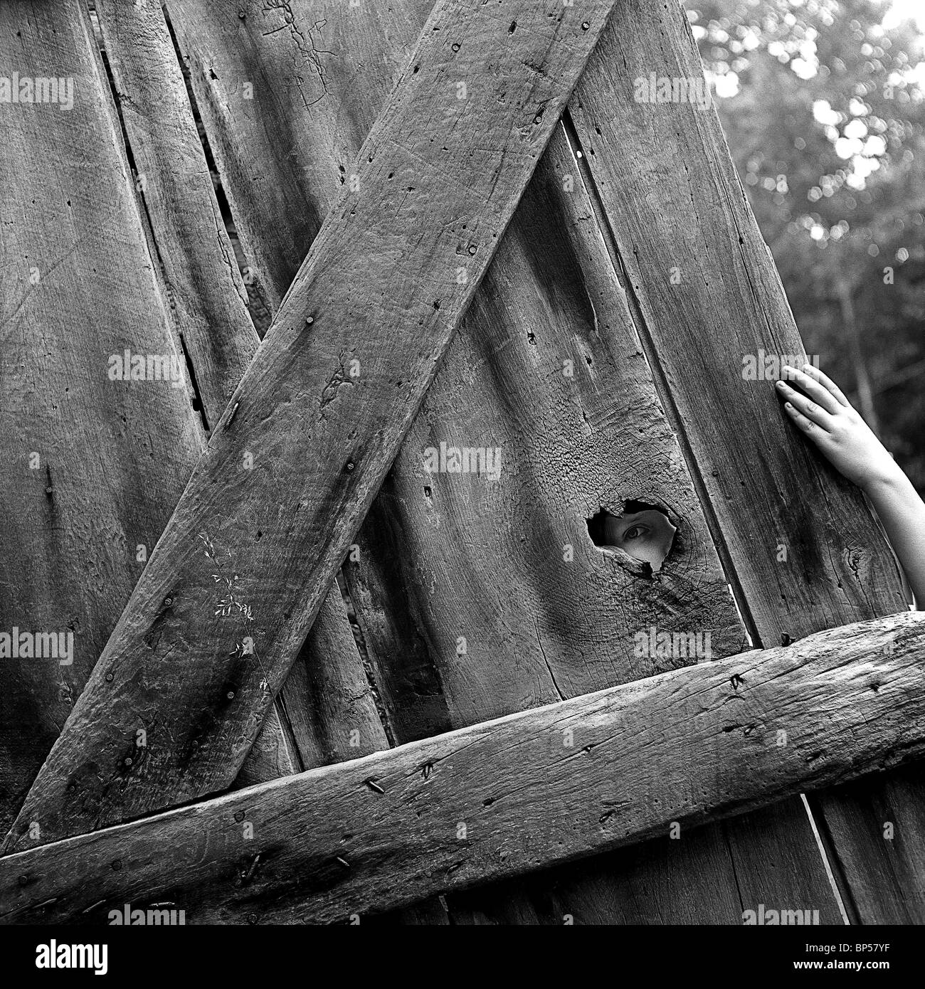 Girl looking through hole in barn door Stock Photo - Alamy