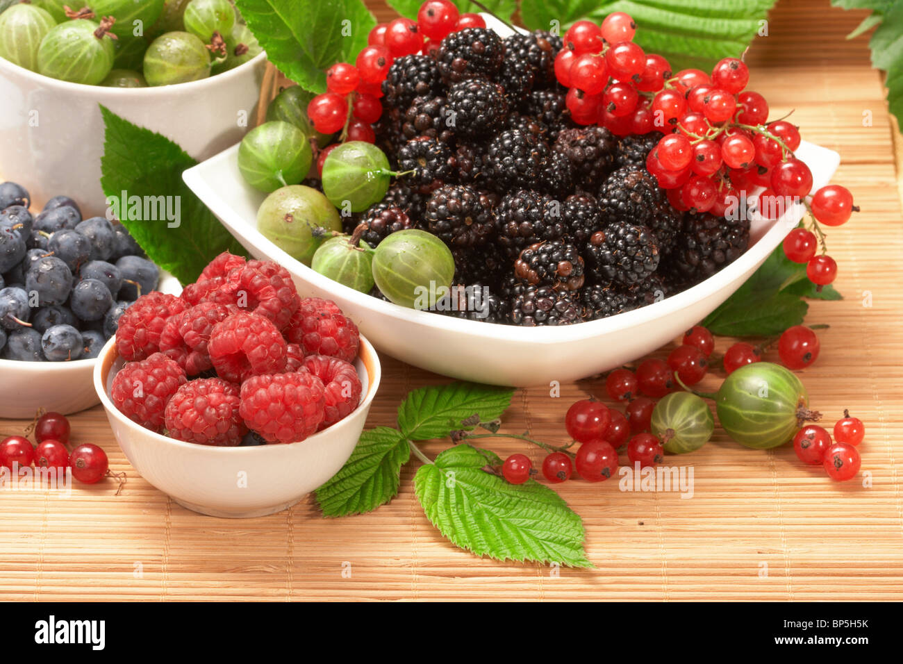 Berries in plates, on a table, among green leaves Stock Photo - Alamy