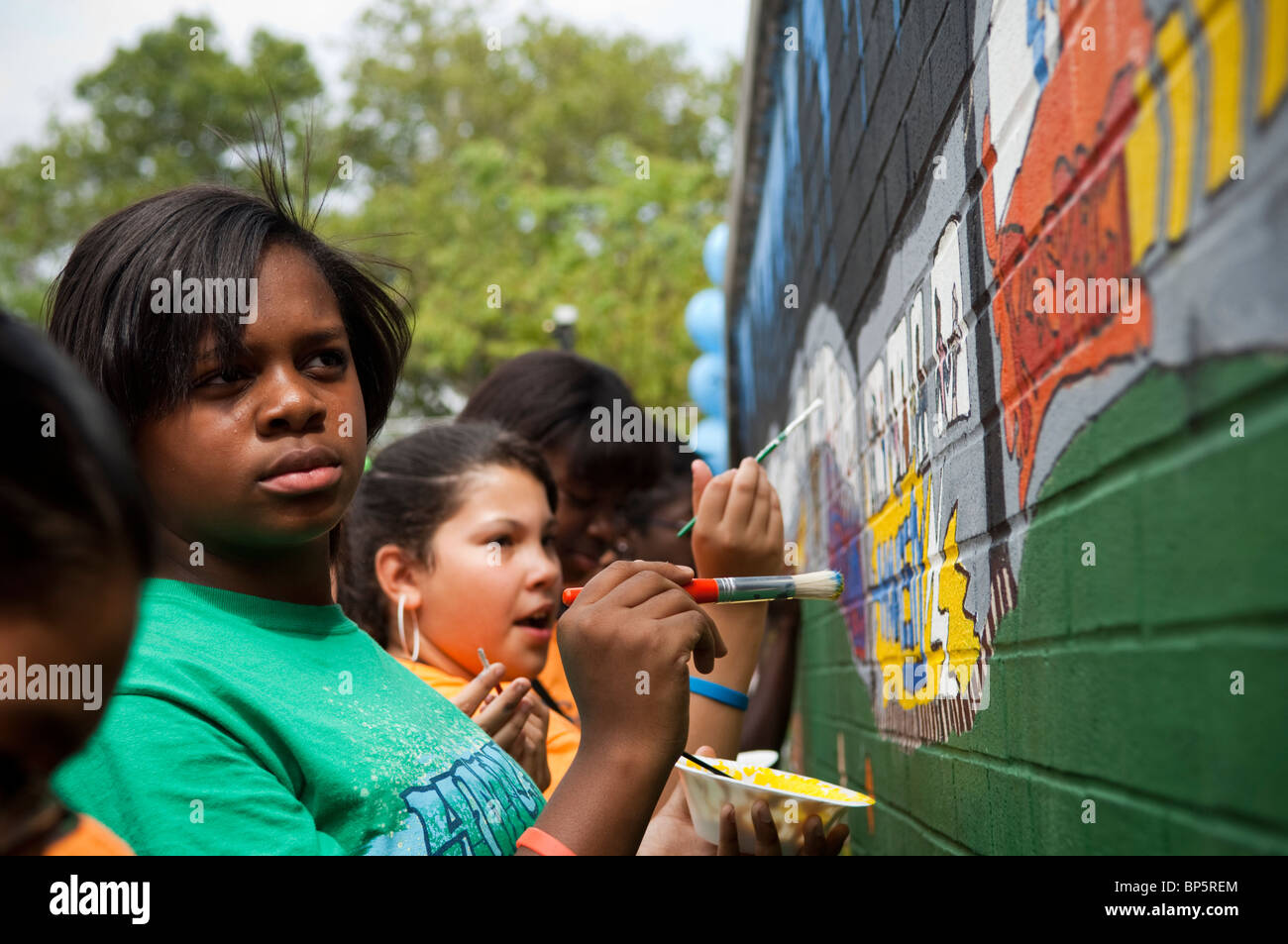 Volunteers and students paint a mural against bullying at a middle ...