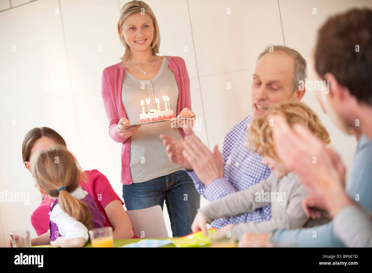 Family at a birthday celebration with a woman bringing cake in the ...