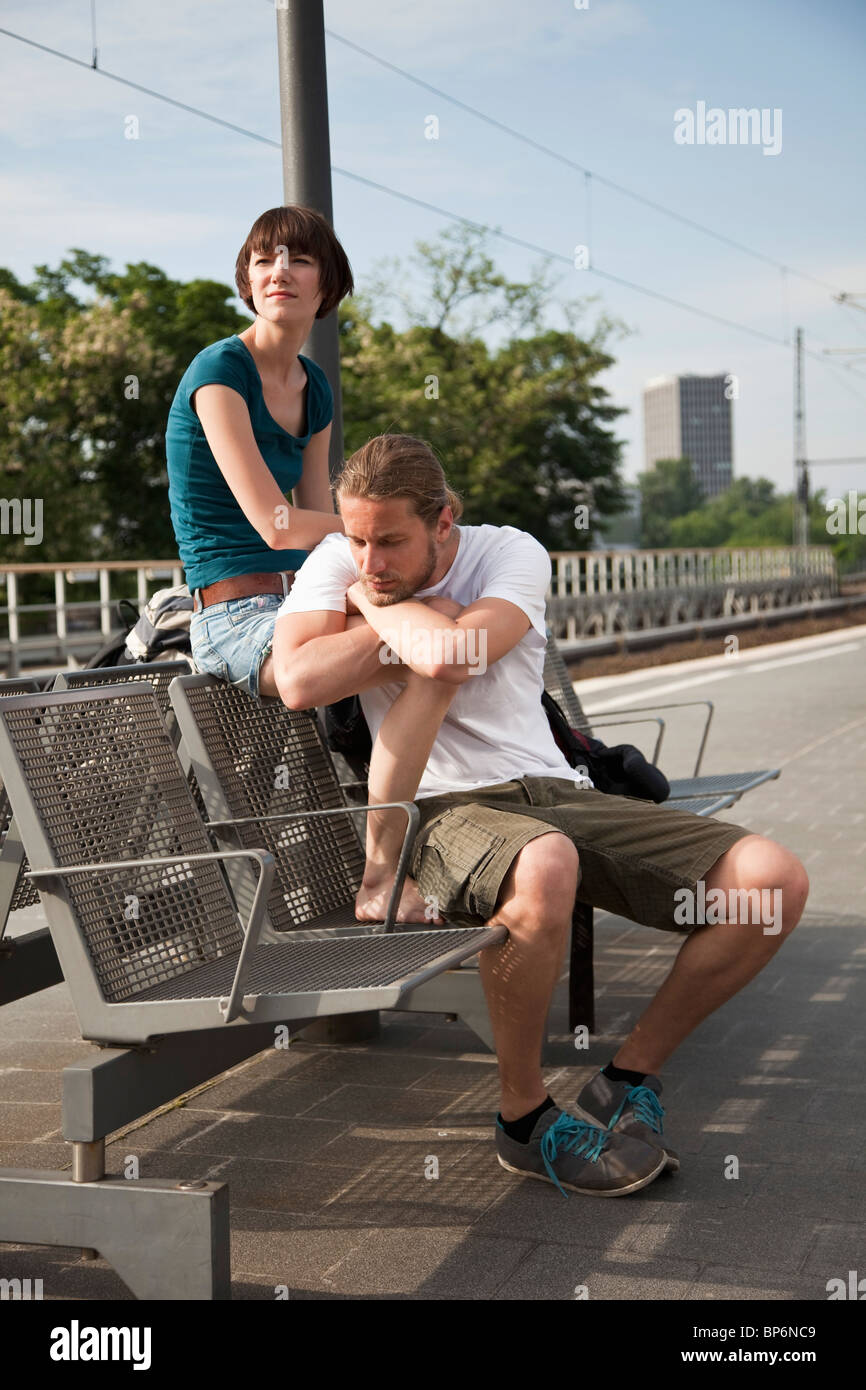 A bored backpacker couple waiting for their train on a train platform ...