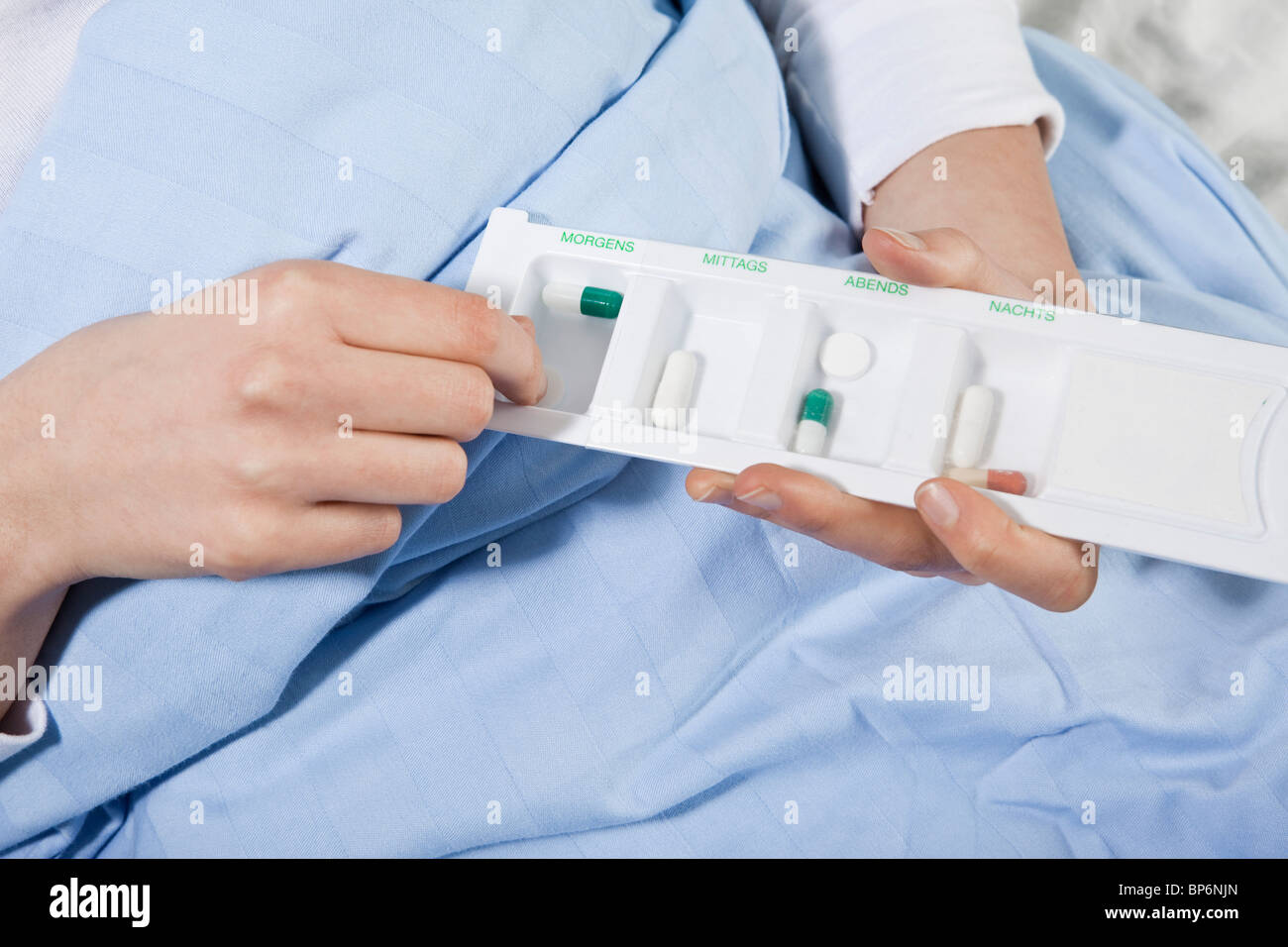 A patient in a hospital bed taking a pill from a pill organizer, focus ...