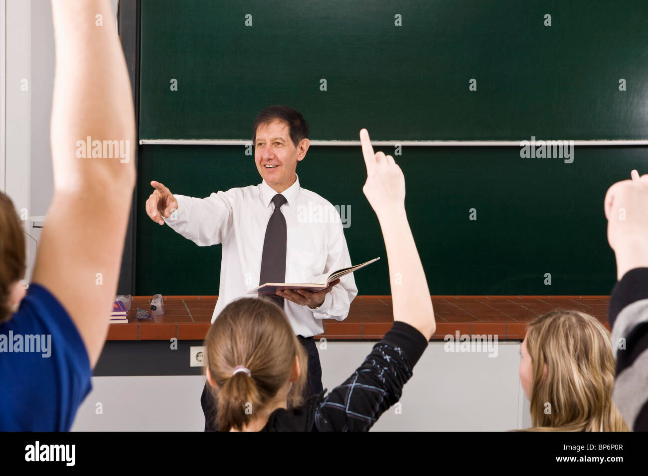 A teacher points while his students raise their hands in a classroom ...