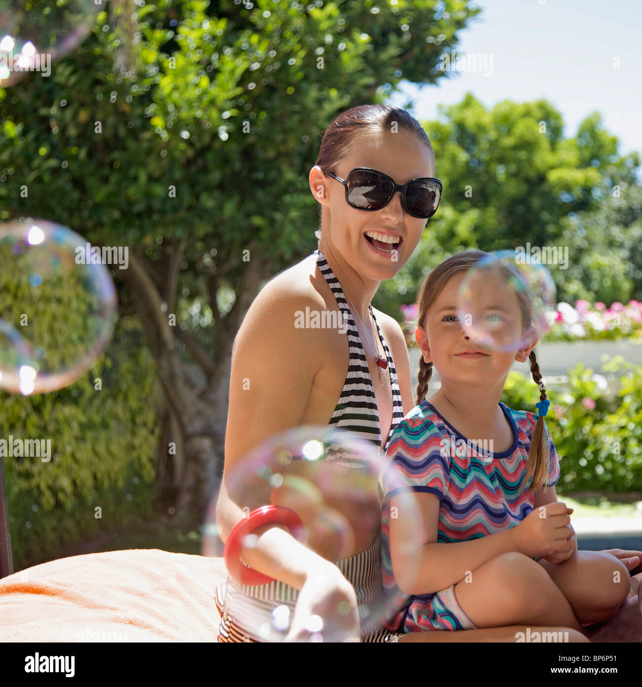 Soap bubbles floating by a mother and daughter sitting together ...