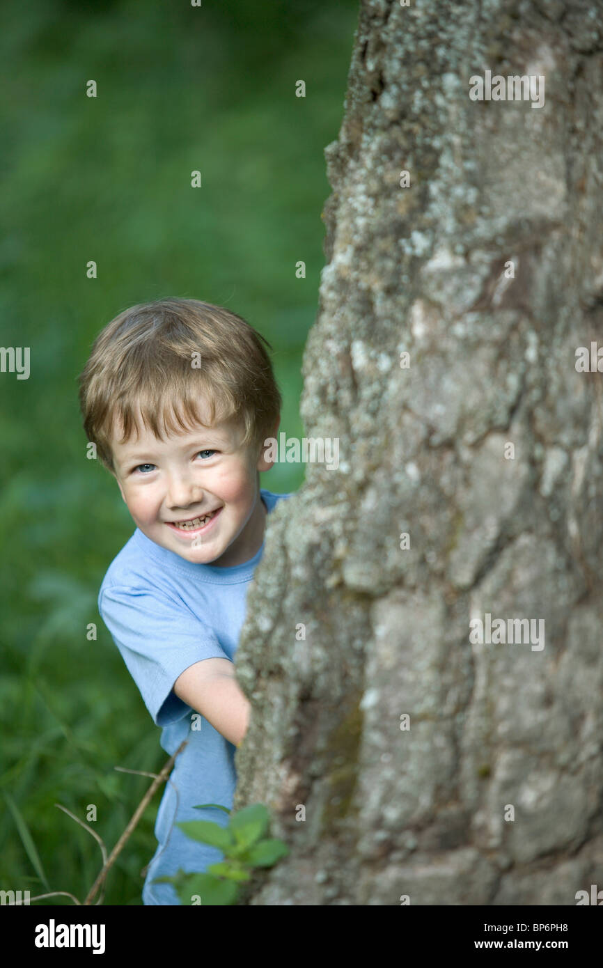 A young boy peeking from behind a tree trunk Stock Photo - Alamy