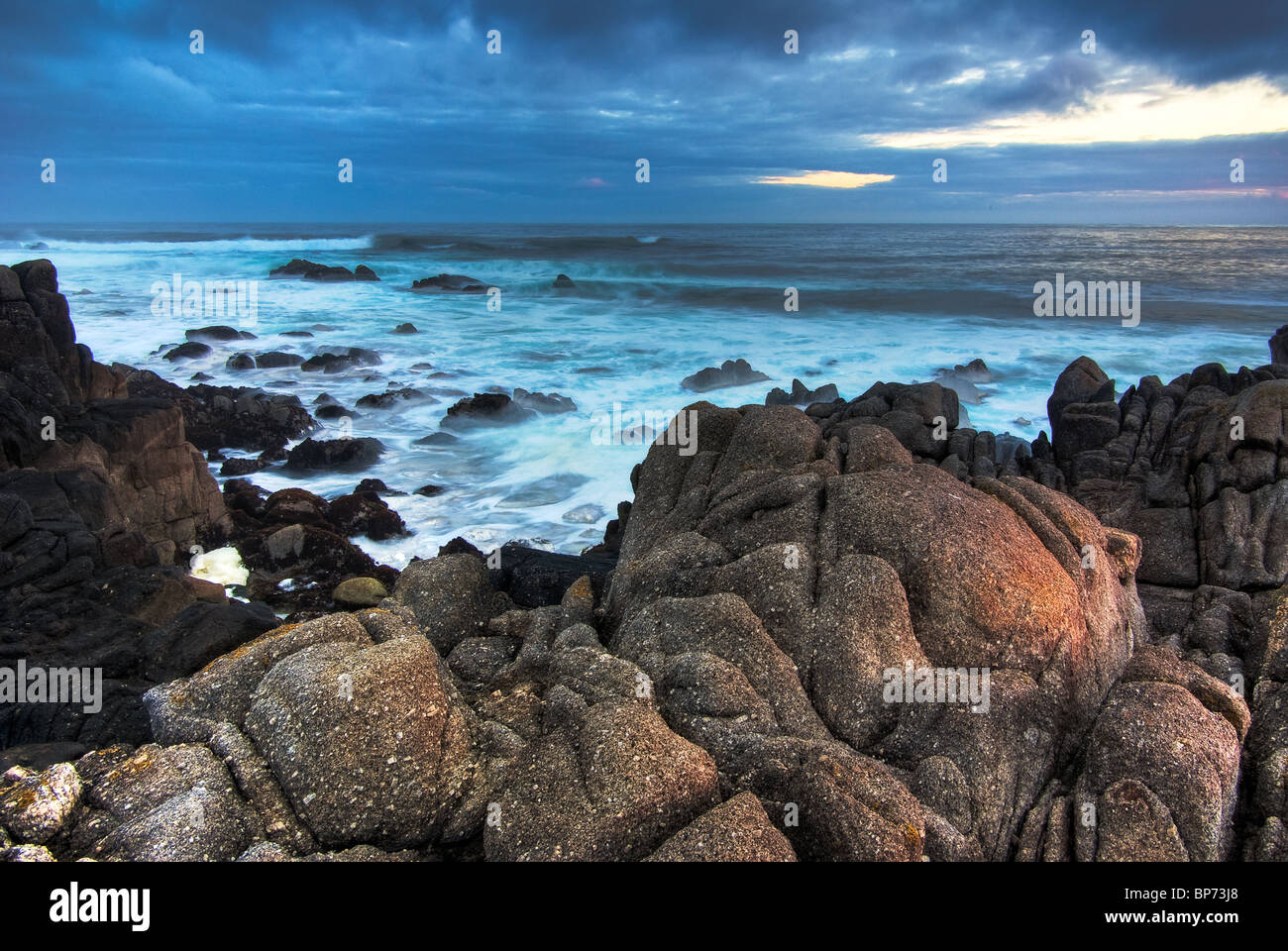 Foreground rocks frame the waves crashing at Monterey at sunrise Stock ...
