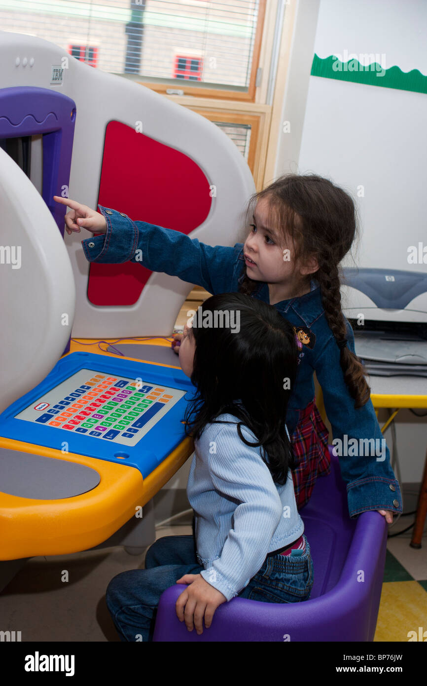 Two 4 year old preschool girls using a computer in the classroom one is ...