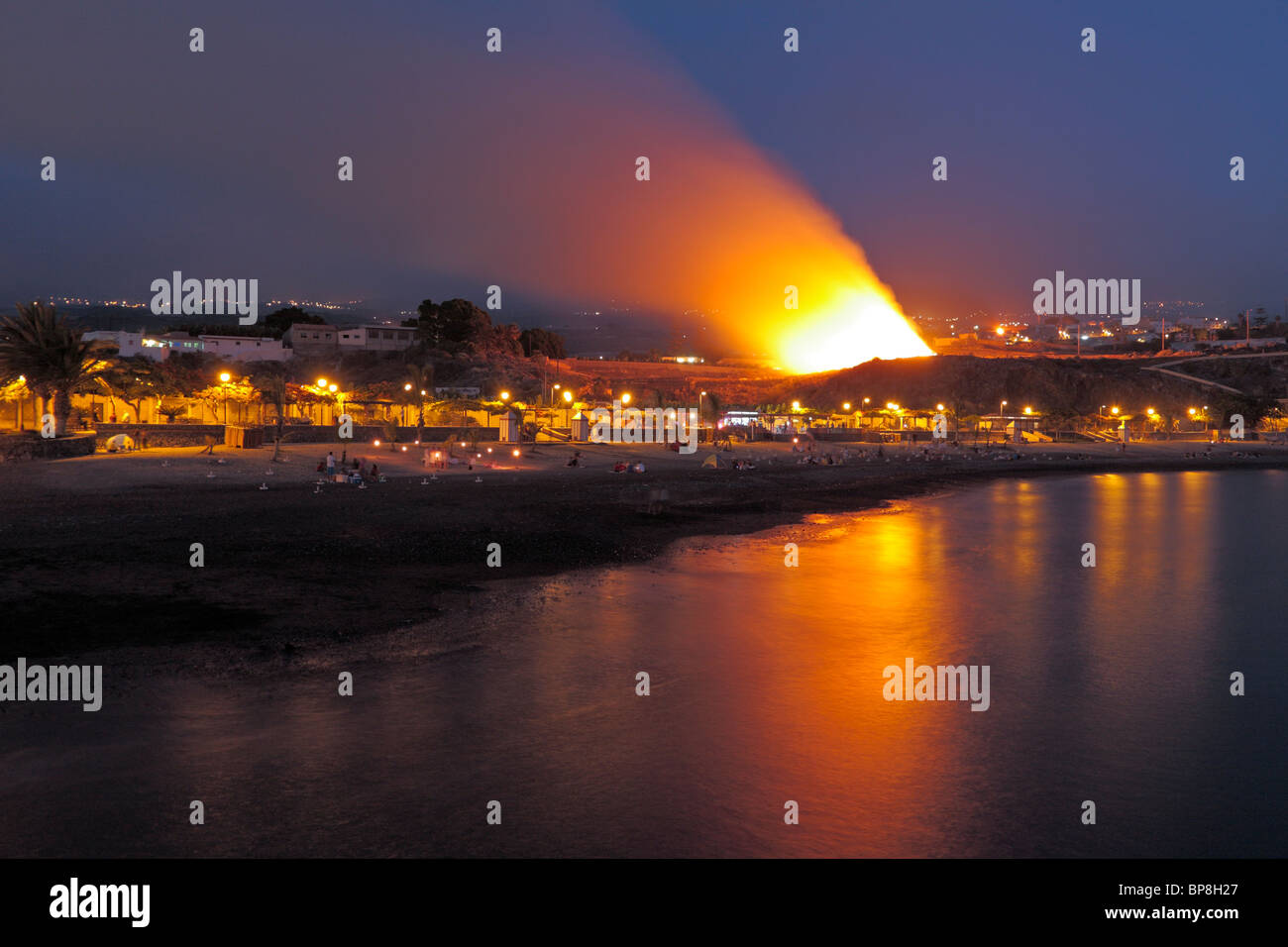 A huge bonfire burns on the cliff above people on the beach celebrating ...