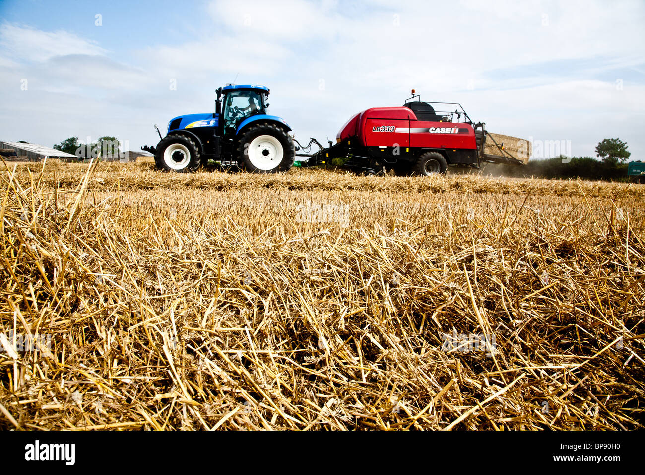 A new Holland tractor, pulling a bailer along, bailing straw Stock ...
