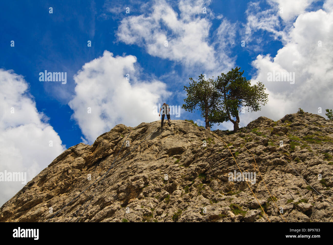 Climber sliding down the rock with blue sky and clouds in background ...