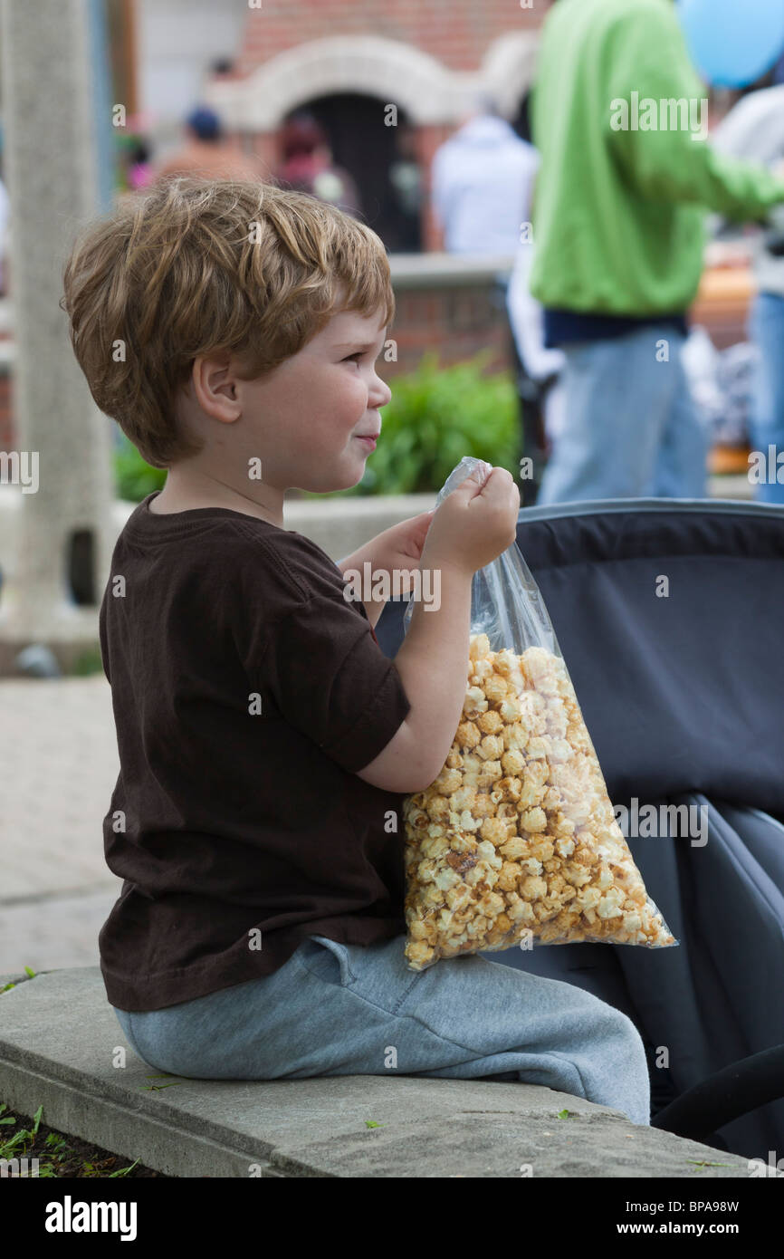 A small child sits alone on the street and eats popcorn corn popping ...
