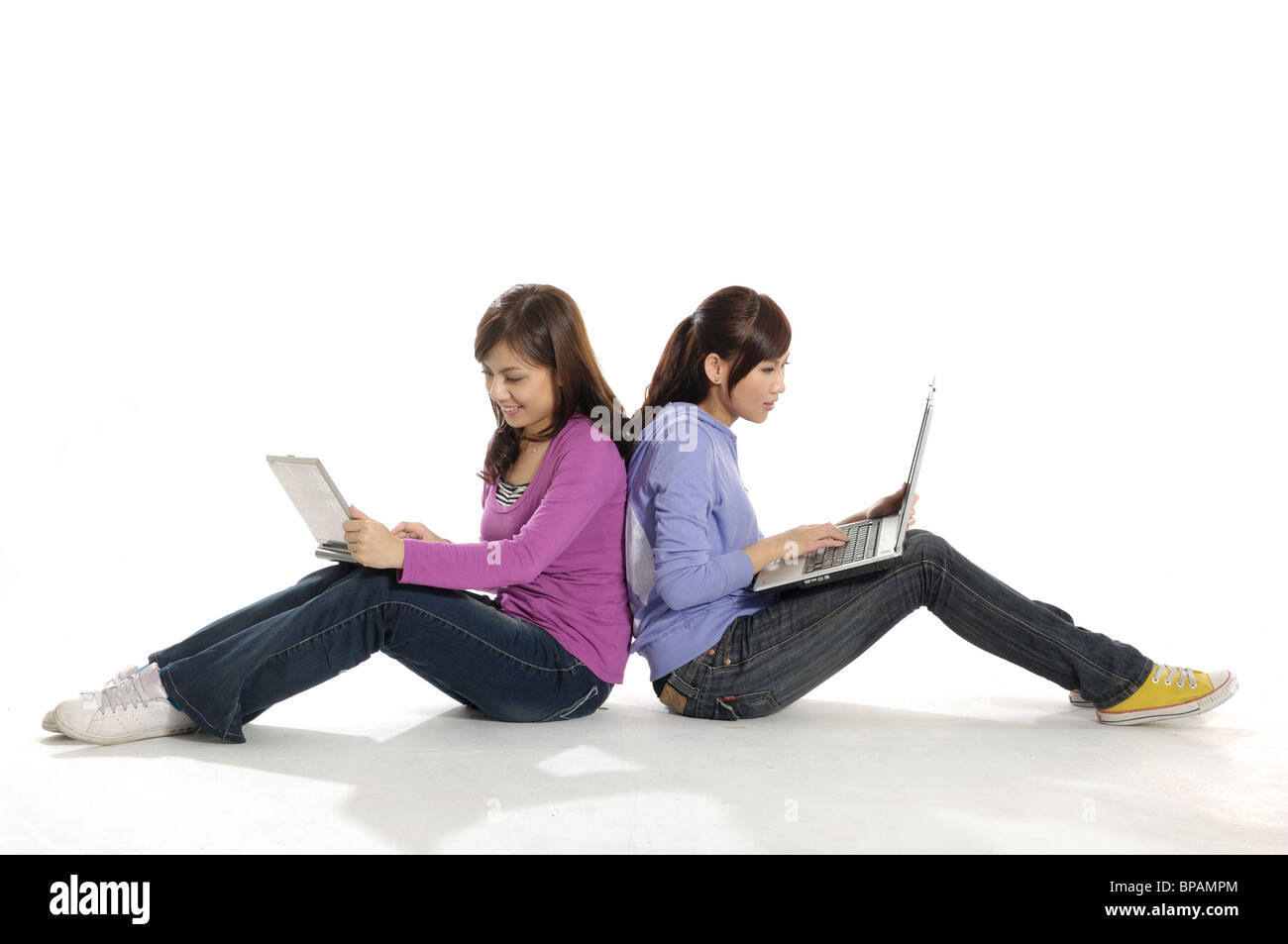 Female university students sitting back to back and using laptops Stock ...