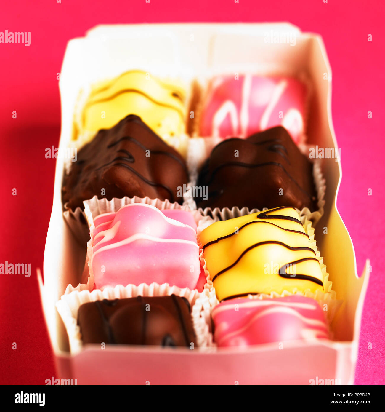 Assorted Fondant Fancies In A Paper Tray On A Pink Background Stock ...