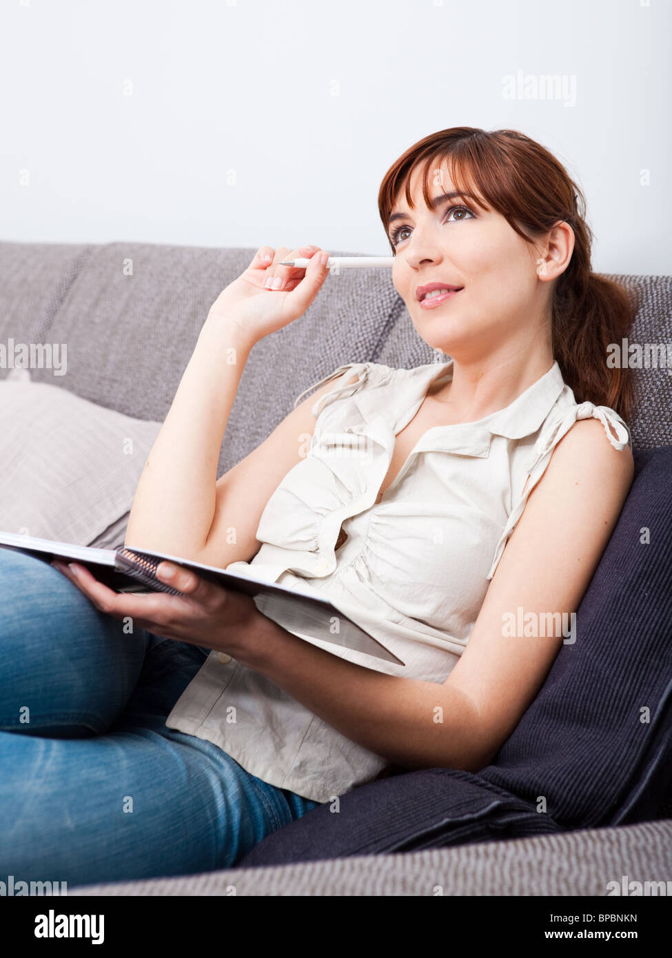 Woman thinking sitting on couch holding a pen and a book Stock Photo ...