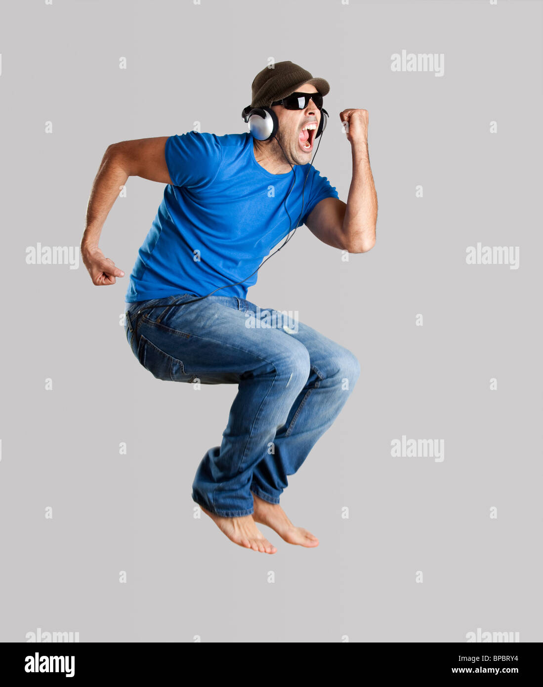 Young man jumping and listening music isolated over a gray background ...