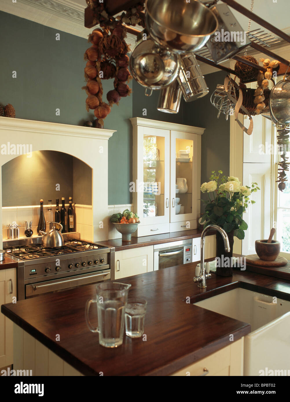 Pans on ceiling-mounted rack above sink in island unit in green kitchen ...